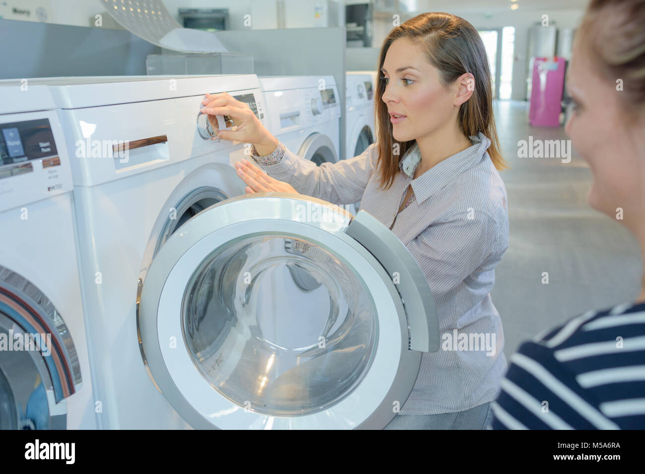 Woman demonstrating washing machine to customer Stock Photo - Alamy