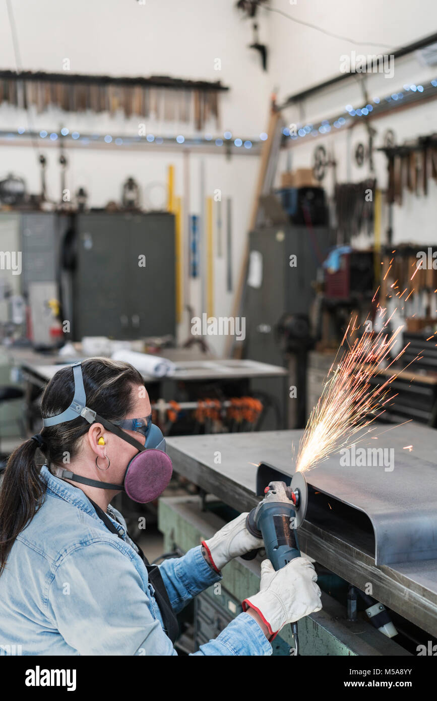 Woman wearing safety glasses and dust mask standing in metal workshop ...