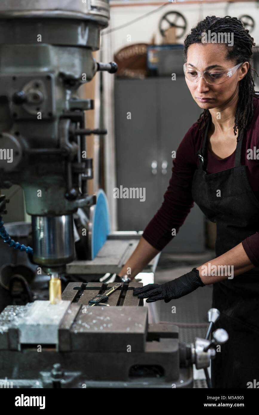 Woman wearing safety glasses standing in a metal workshop, working at a ...