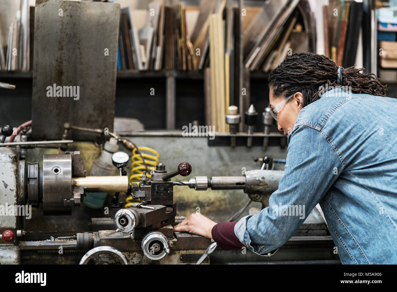 Woman wearing safety glasses standing in a metal workshop, working at a ...