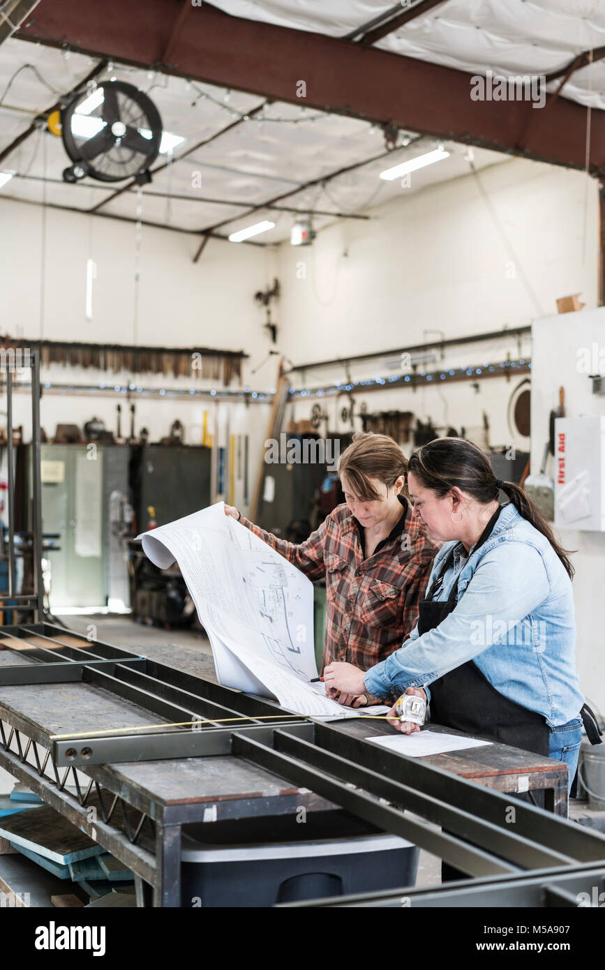 Two women standing at workbench in a metal workshop, looking at ...