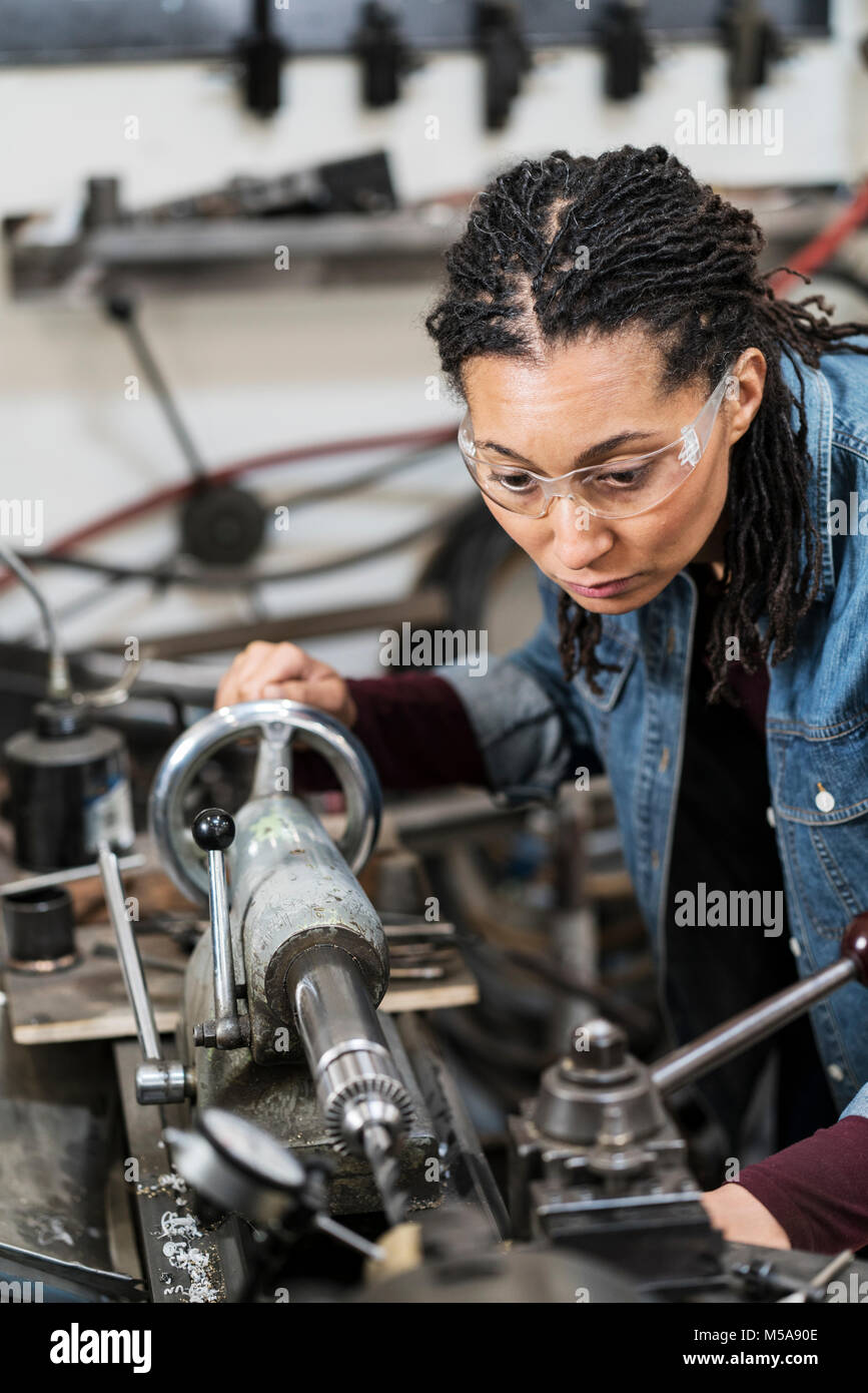 Woman wearing safety glasses standing in a metal workshop, working at a ...