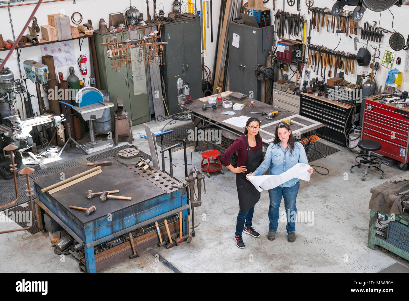 High angle view of two women standing in metal workshop, holding ...