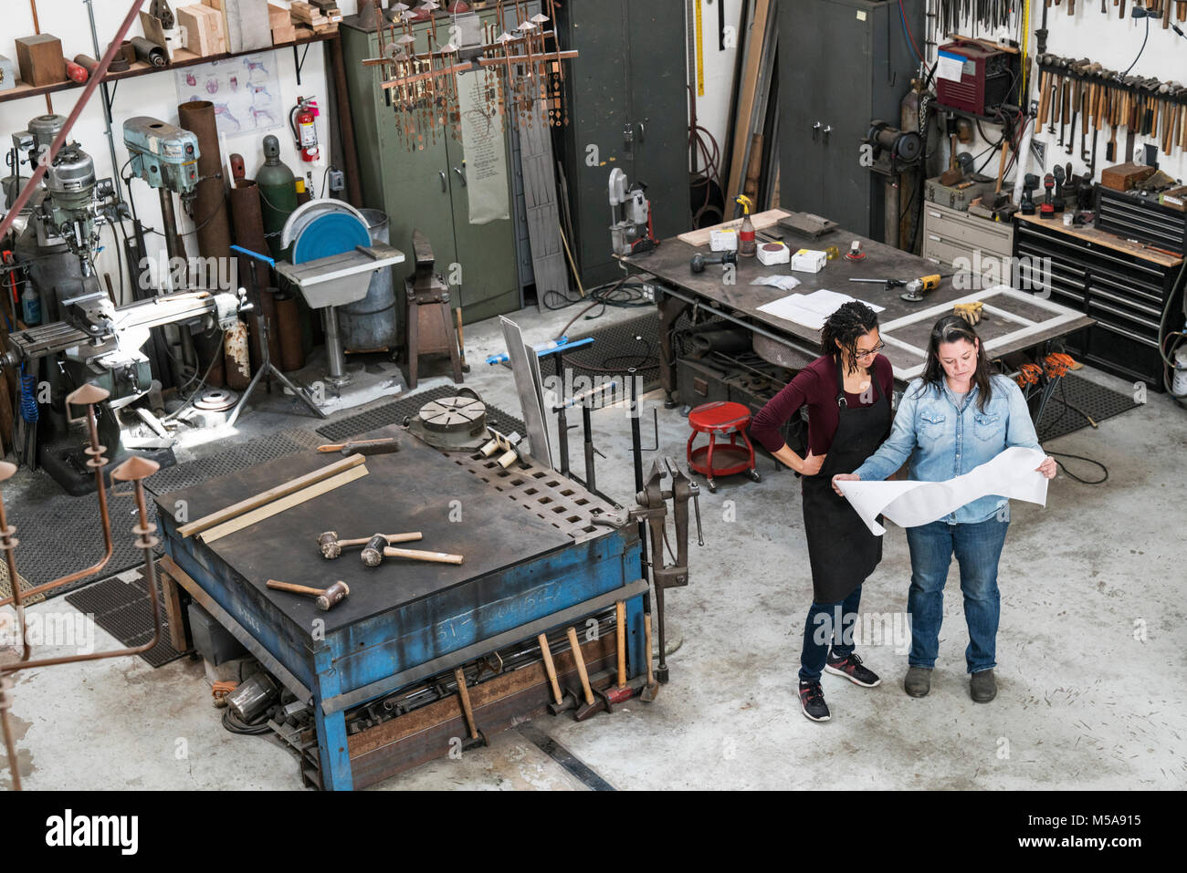 High angle view of two women standing in metal workshop, holding ...