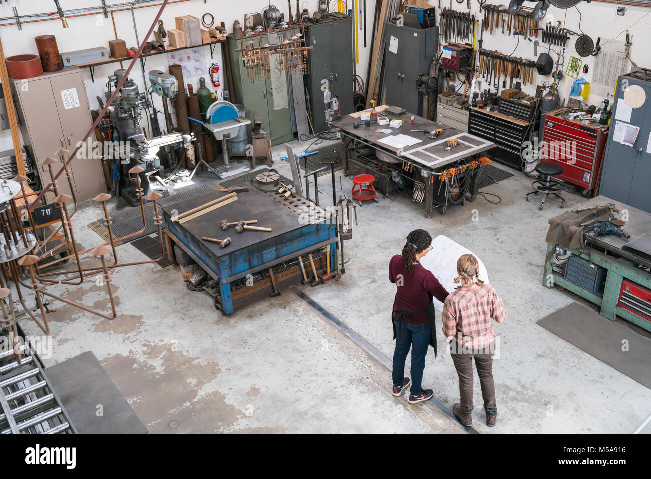 High angle view of two women standing in metal workshop, holding ...