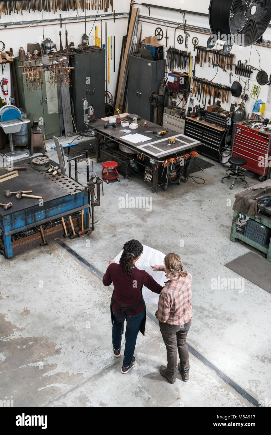 High angle view of two women standing in metal workshop, holding ...