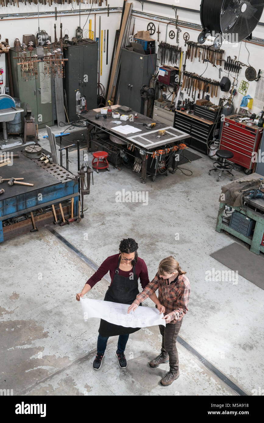 High angle view of two women standing in metal workshop, holding ...