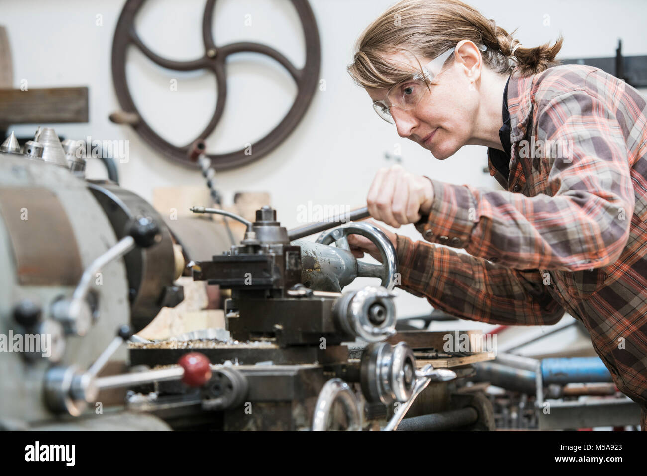 Woman wearing safety glasses standing in a metal workshop, working at ...