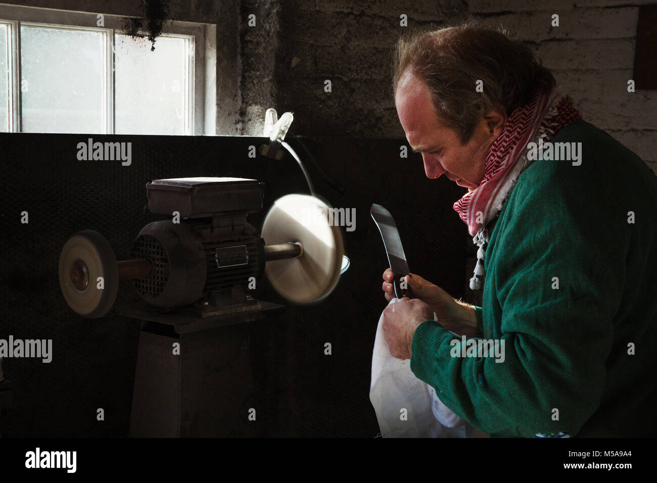 Craftsman in a workshop, holding a knife with a large blade inspecting ...