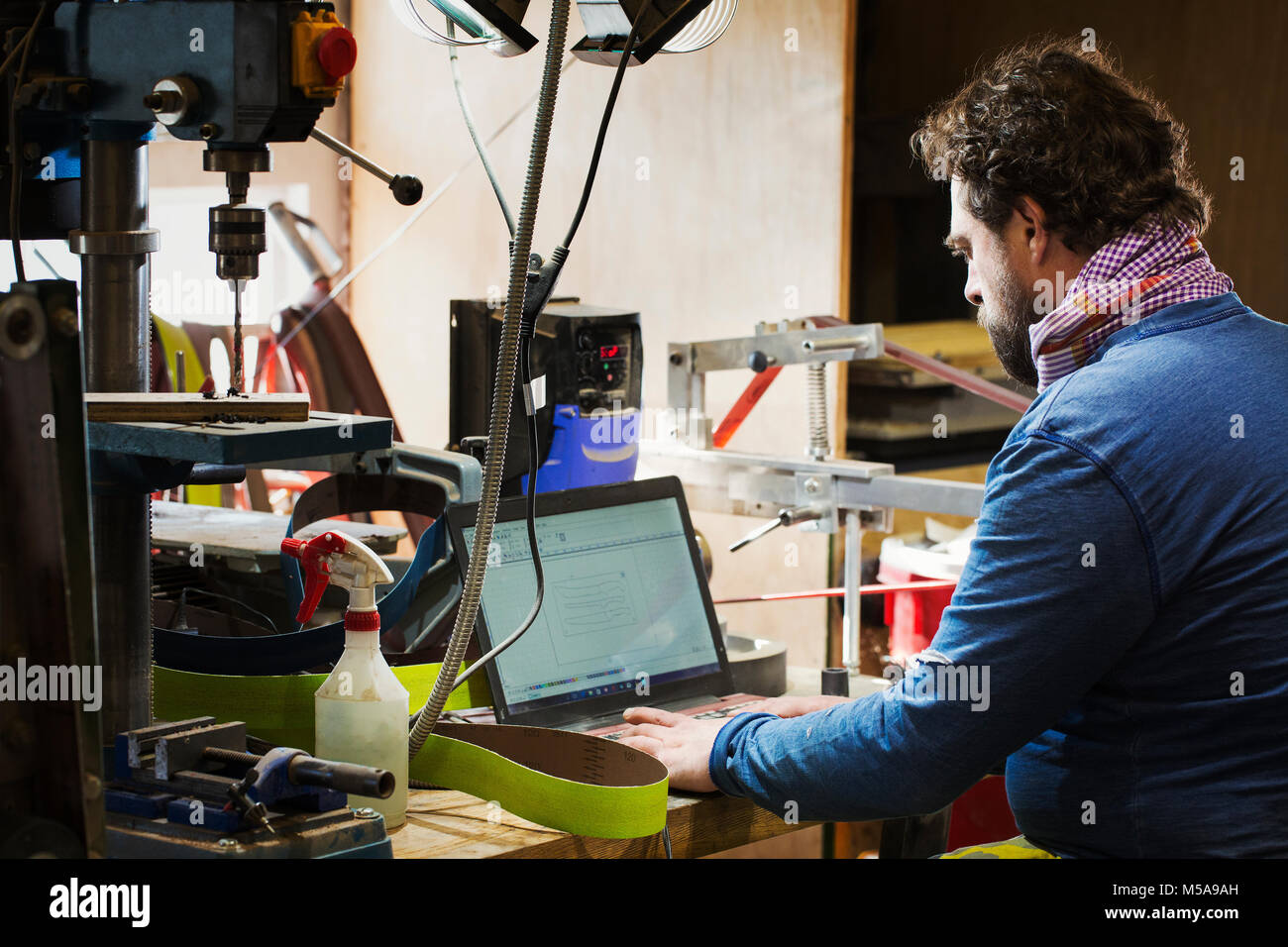 A craftsman at a desk in a workshop using a laptop computer on a ...
