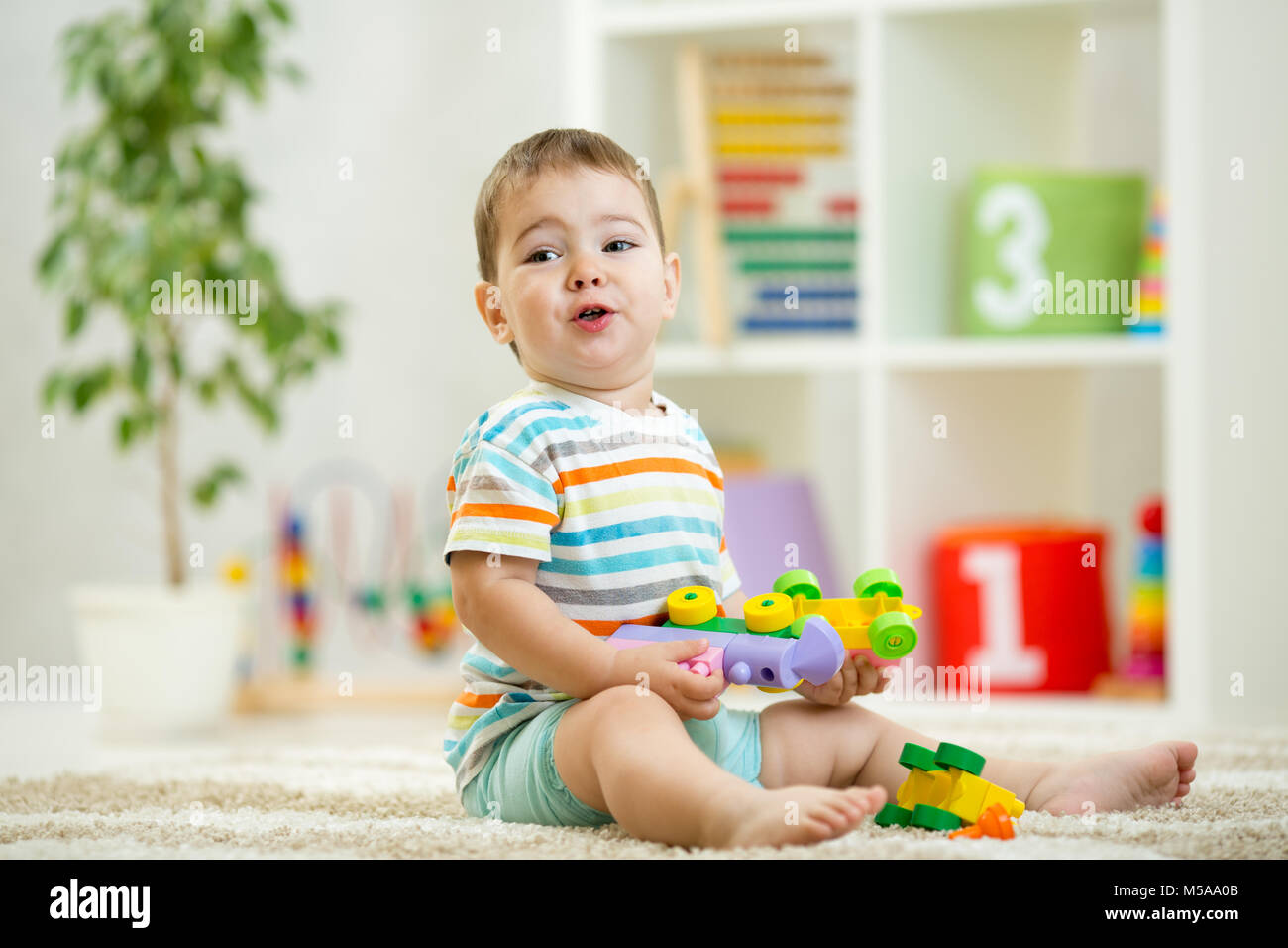 Happy child playing with colorful plastic bricks on the floor. Toddler ...