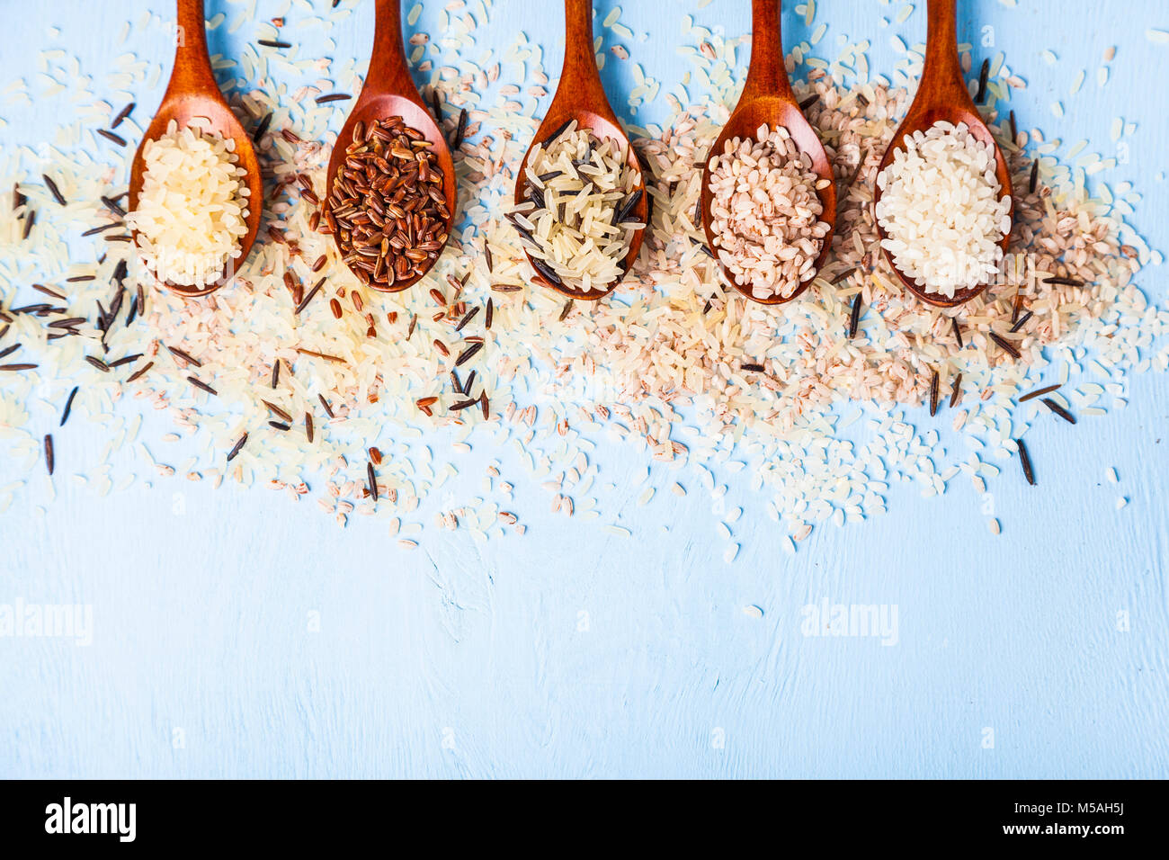 Five spoons with different grades of rice on an old wooden background ...