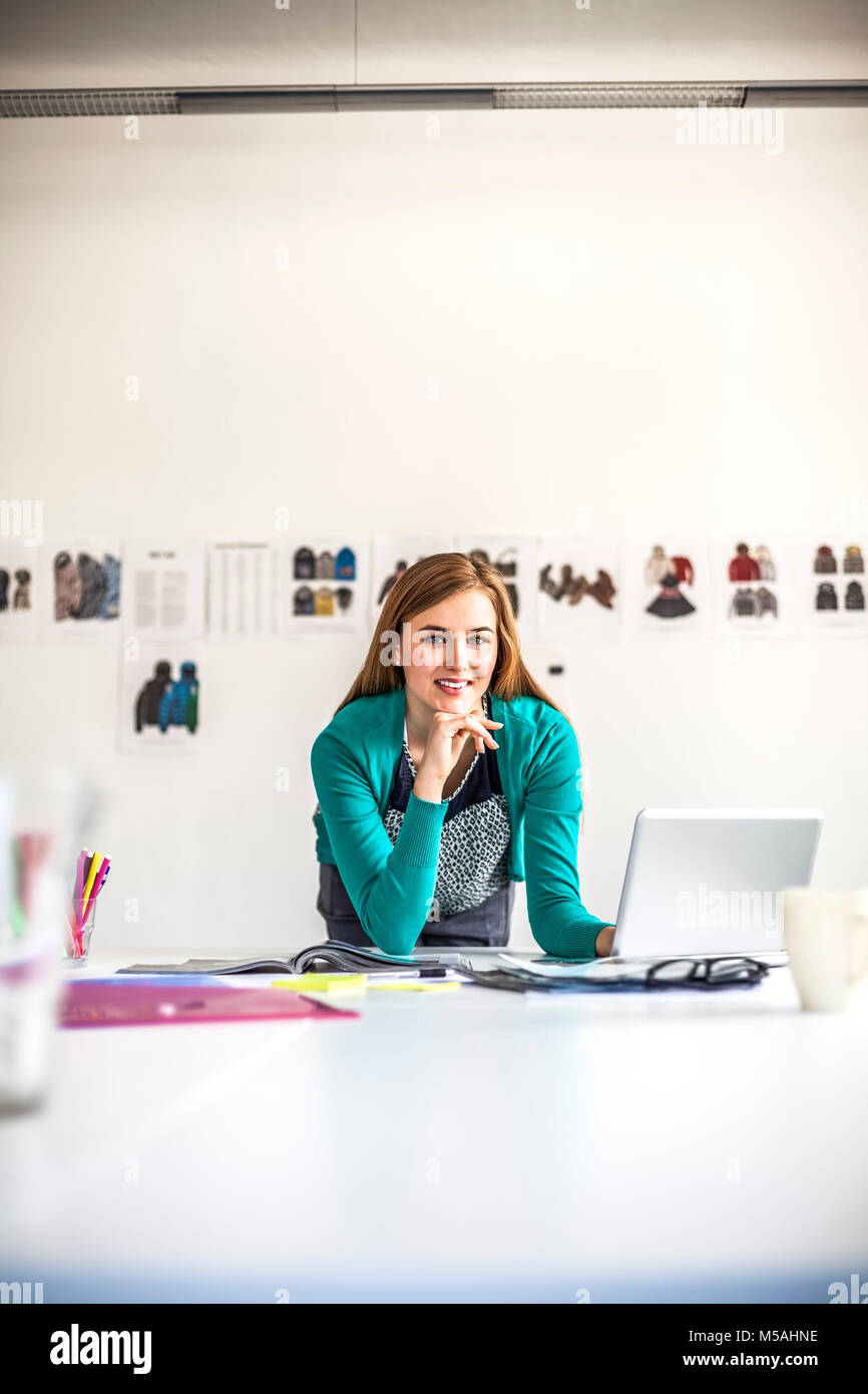 Portrait of confident young female fashion designer with laptop in ...