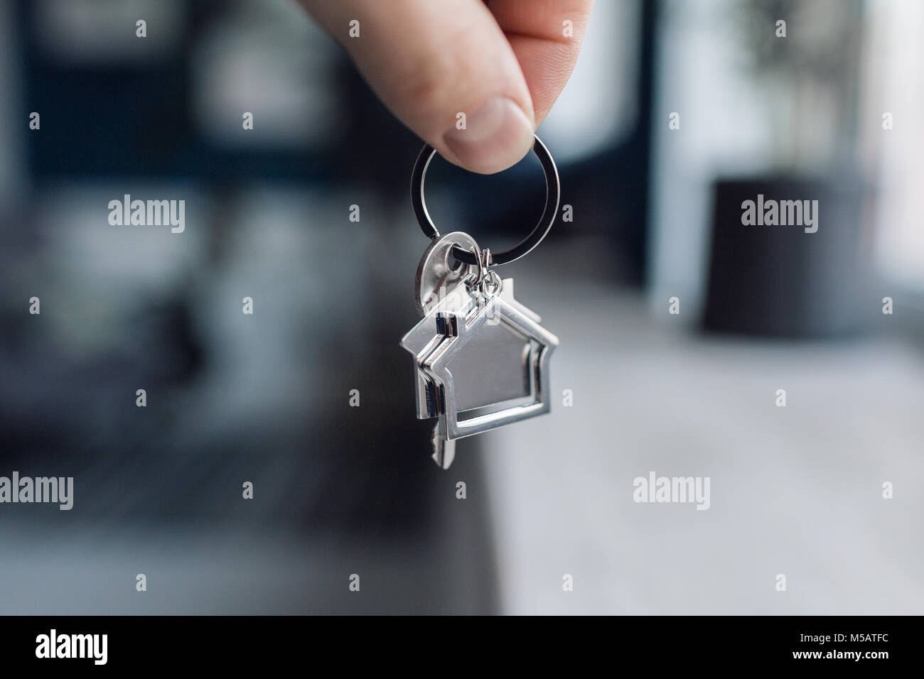 Men hand holding key with house shaped keychain. Modern light lobby ...