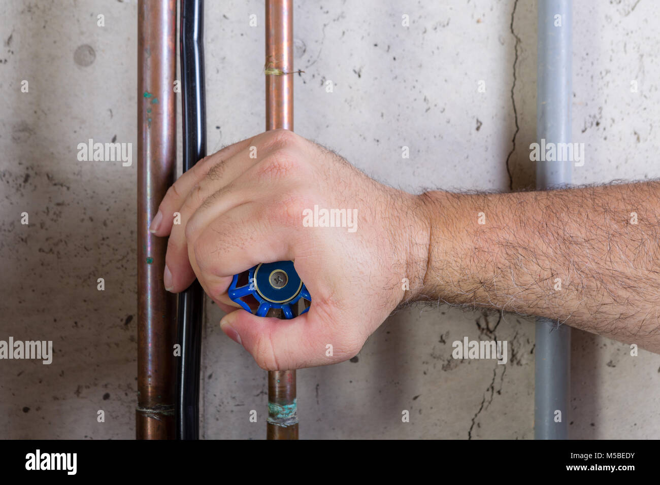 Man using strength to turn a water valve on a pipe gripping it with his ...