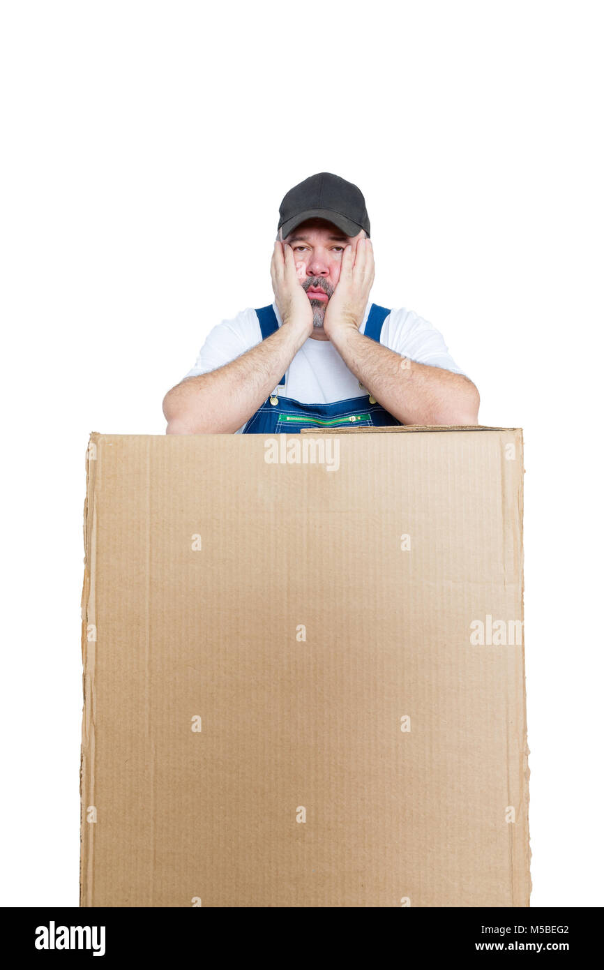 Unhappy delivery man leaning against large package on white background ...