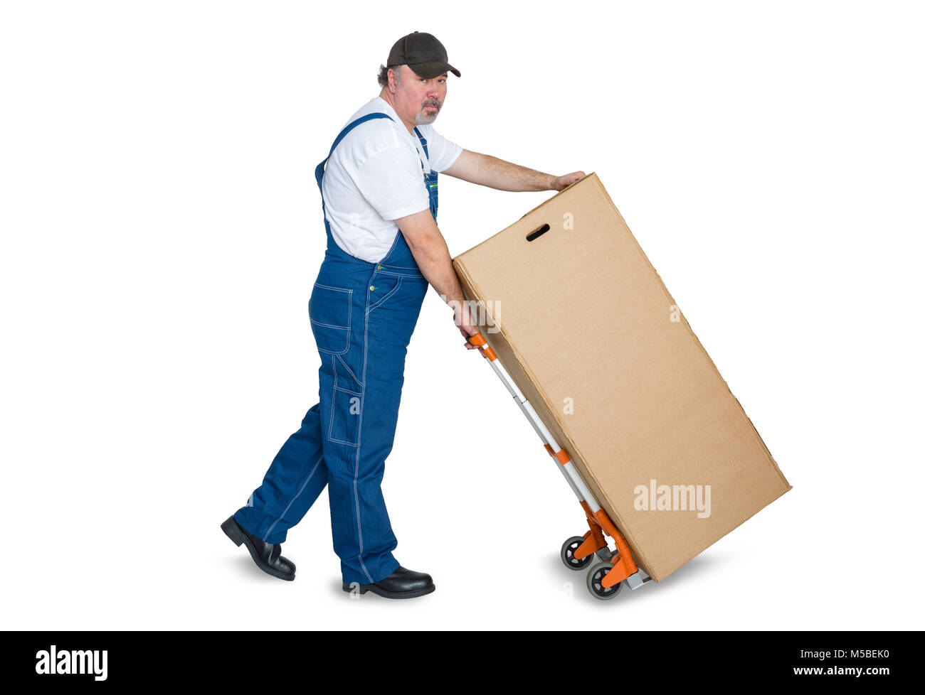 Male worker transporting large cardboard box with trolley against white ...