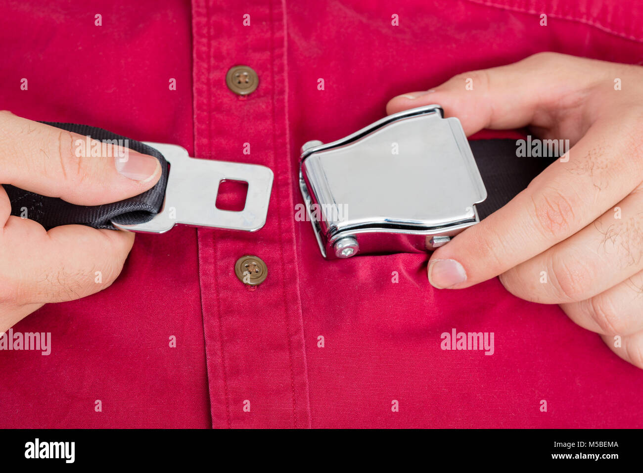 Male passenger on a plane buckling up a seatbelt in a close up view of ...