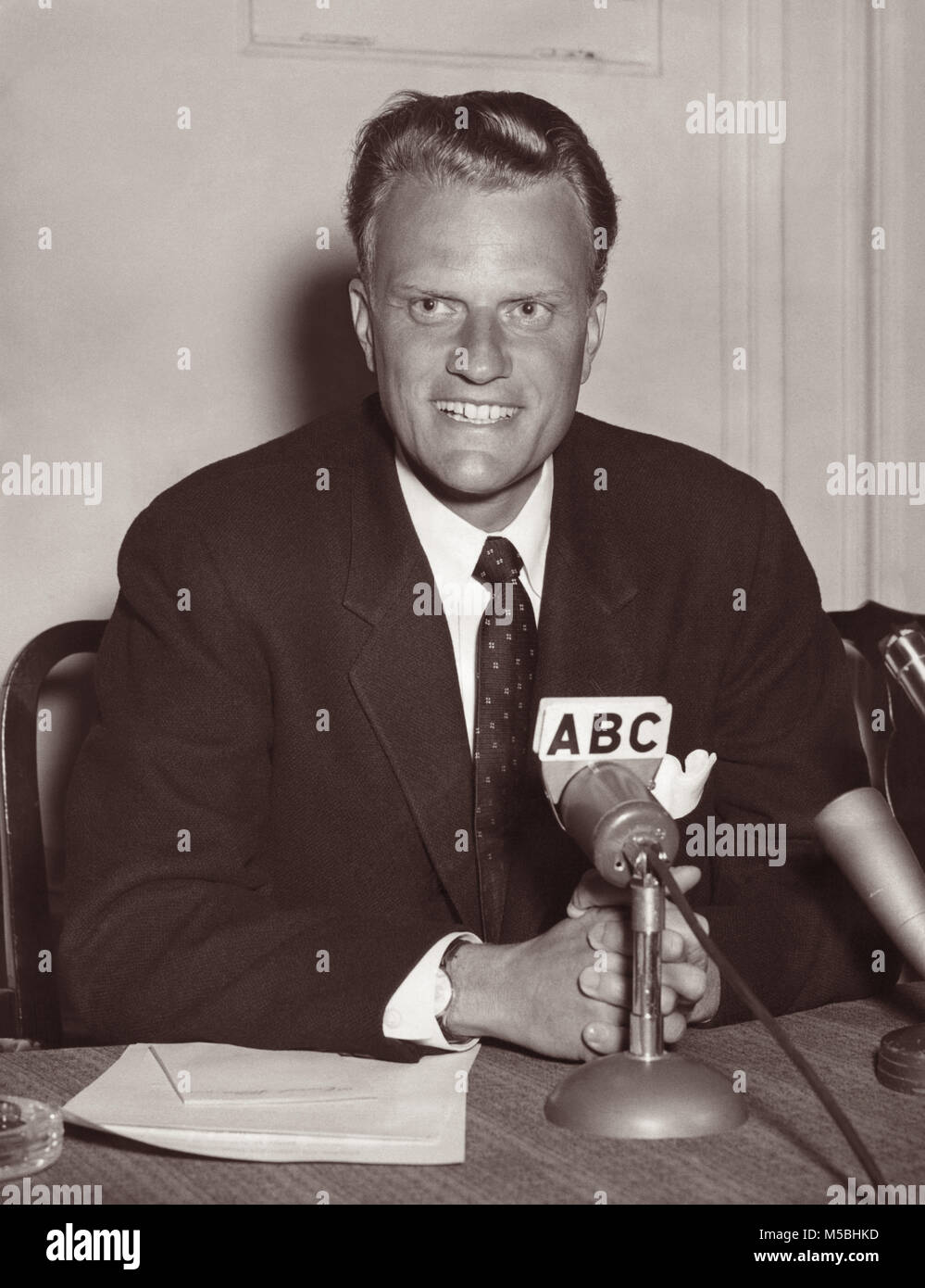 American evangelist Billy Graham (1918-2018) sitting at desk with media ...