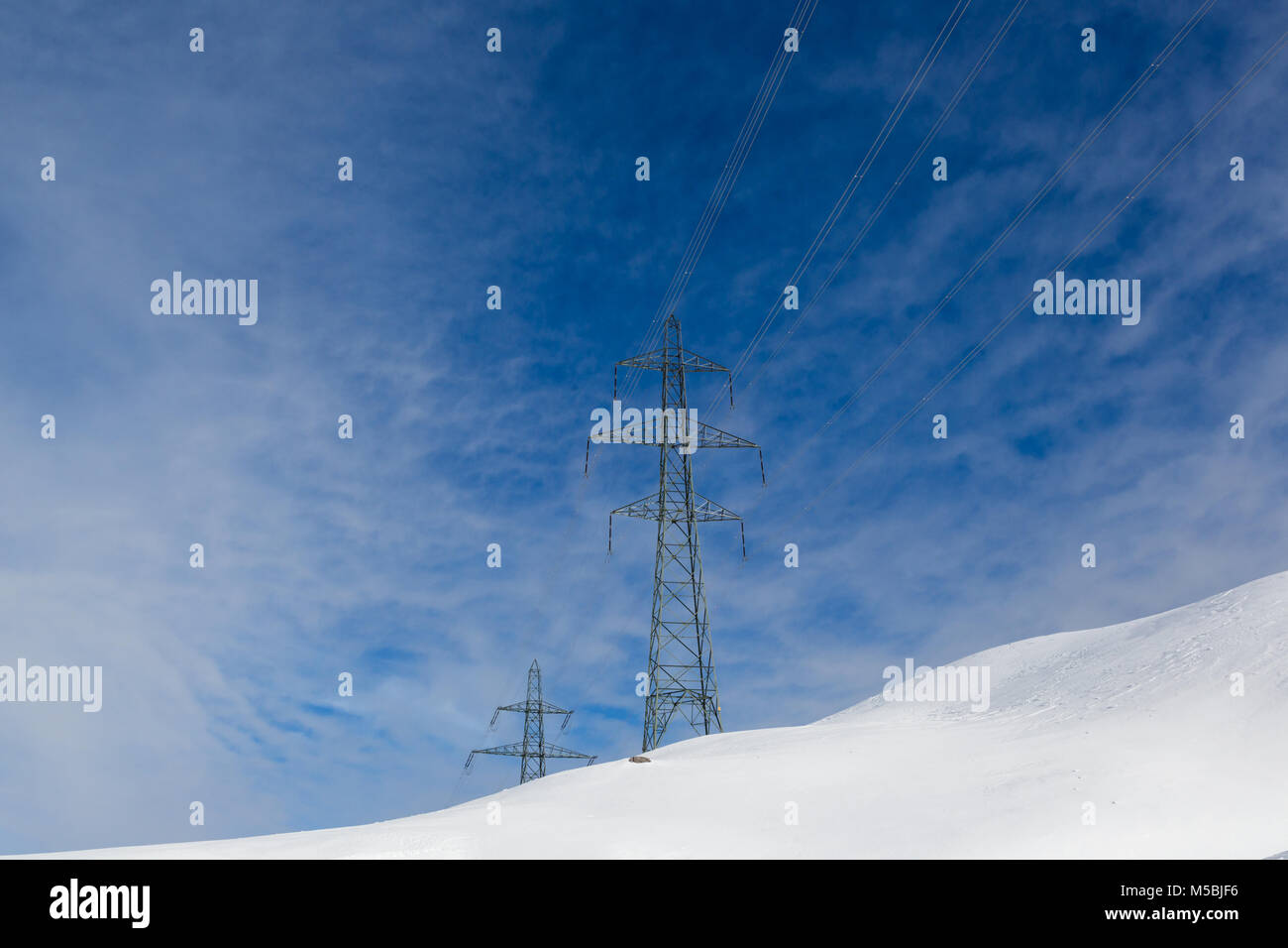 two electricity pylons in winter, white snow, sunny blue sky, clouds ...