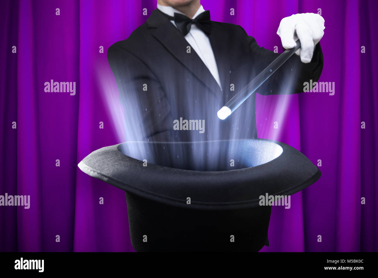 Close-up Of Magician Holding Magic Wand Over Illuminated Hat Against ...
