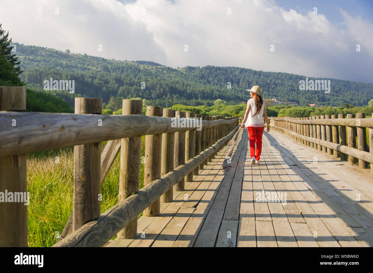 young woman walking on the wooden path along the lake shore. There is a ...