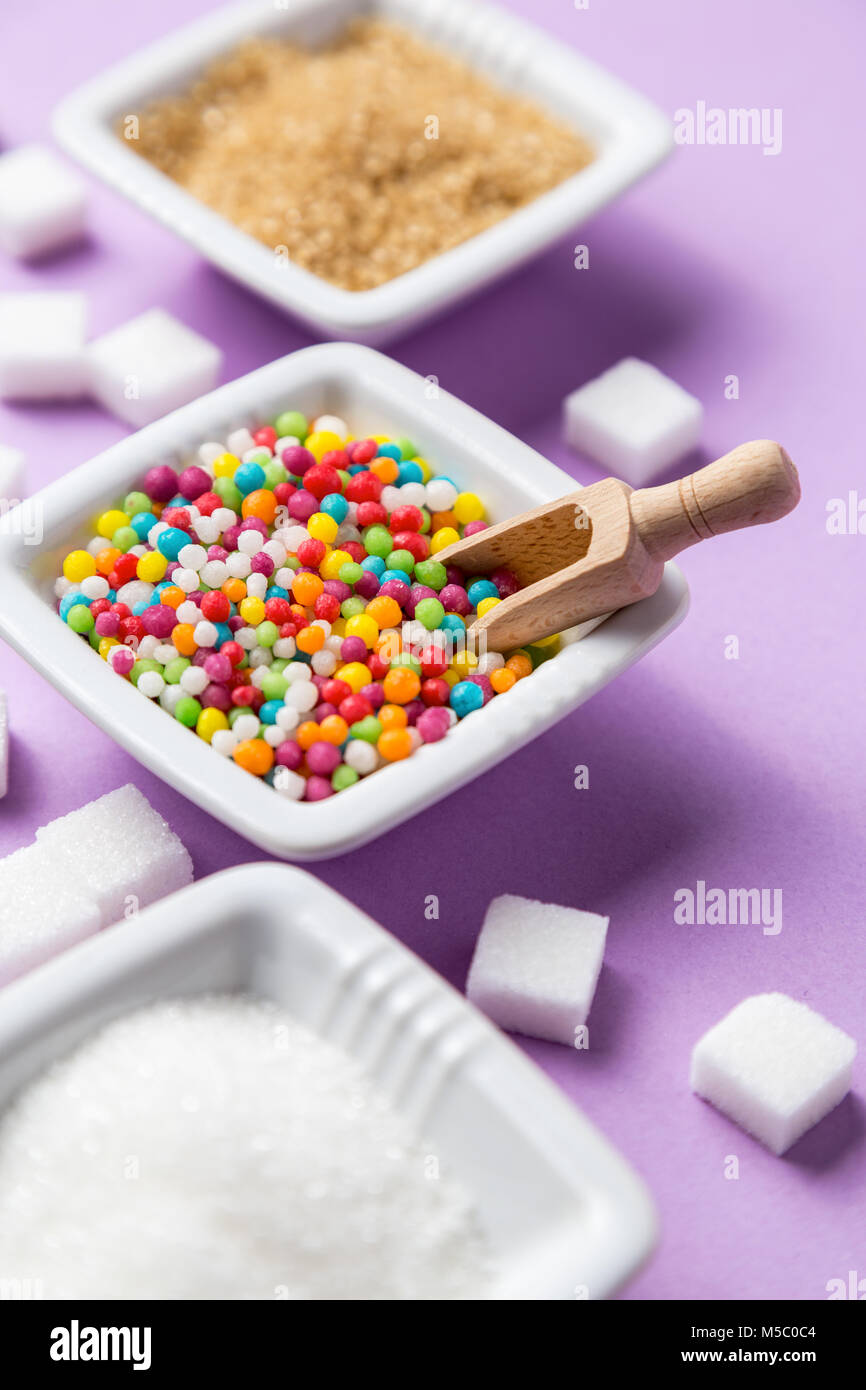 Different types of sugar with colored candy on white ceramic bowls ...