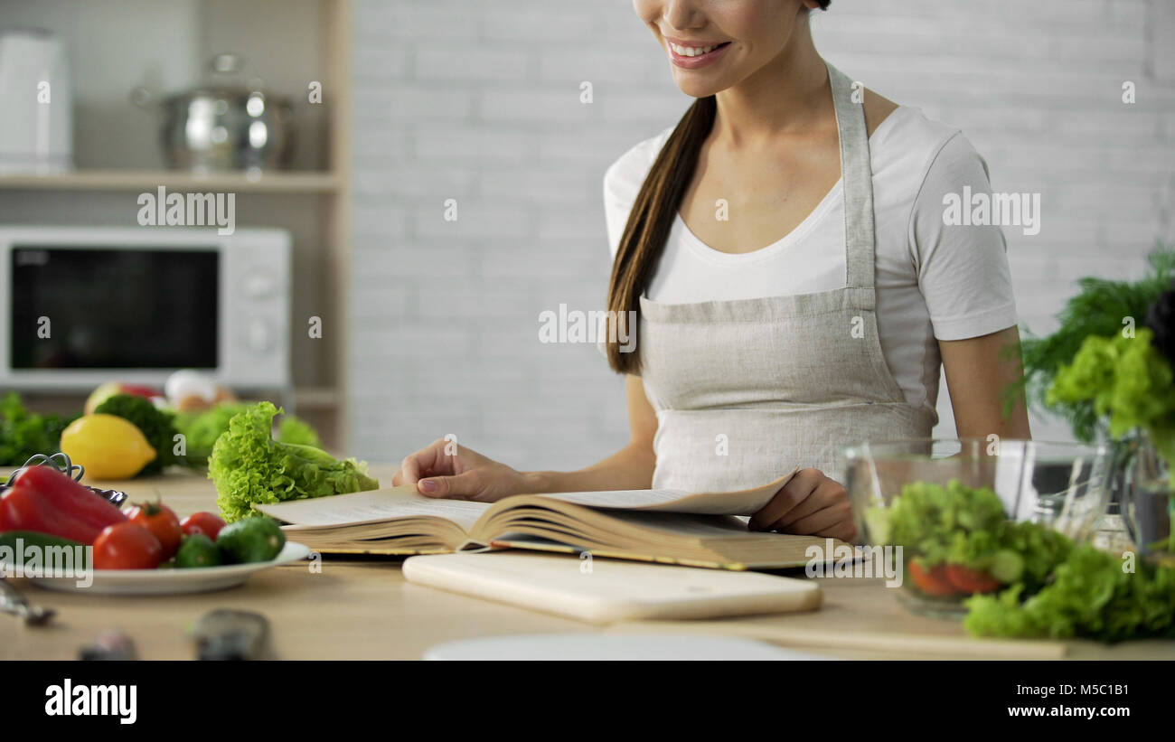 Asian female reading ingredients list for salad in cooking book at home ...