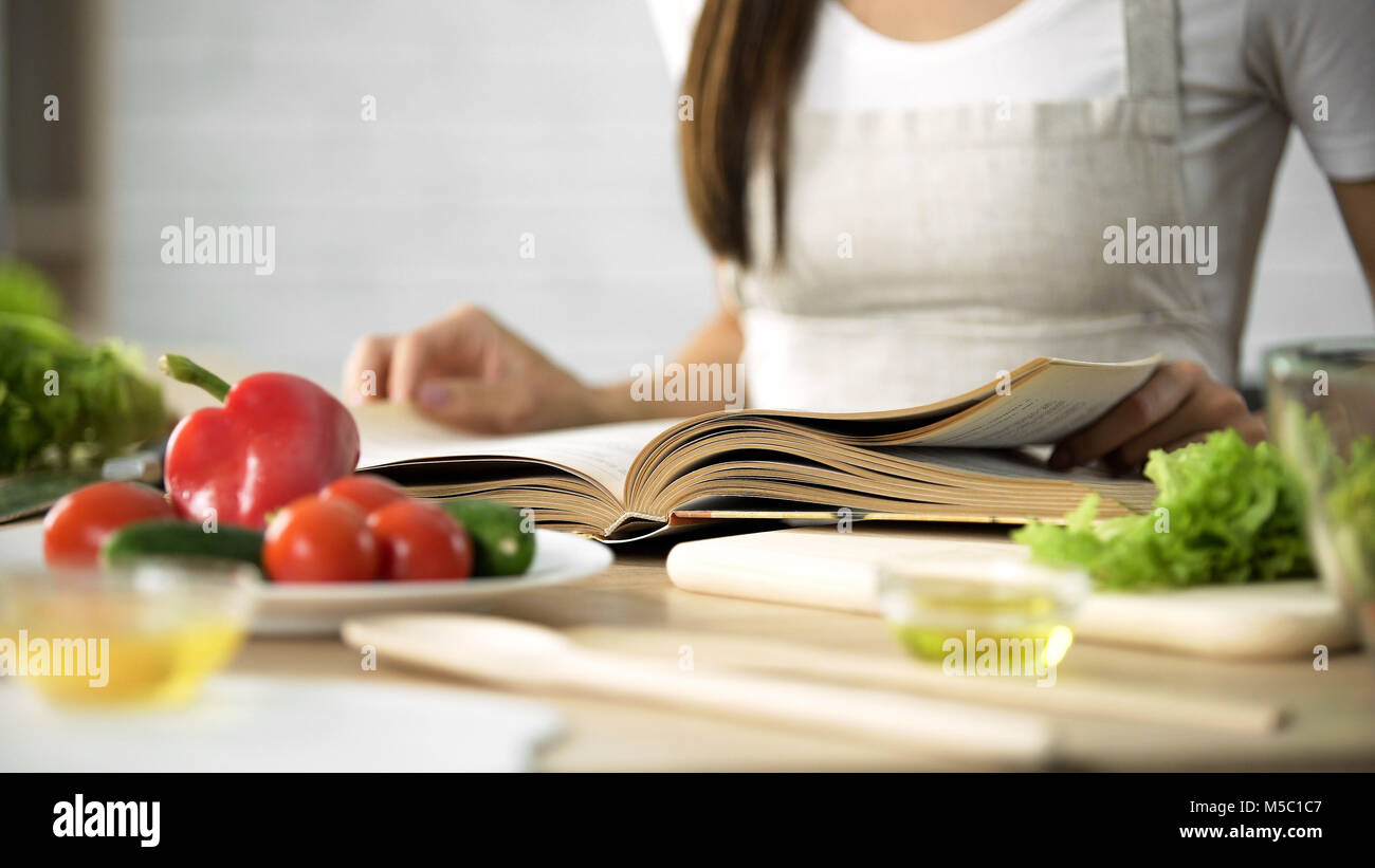 Housewife reading cooking book with fresh vegetables and kitchen tools ...