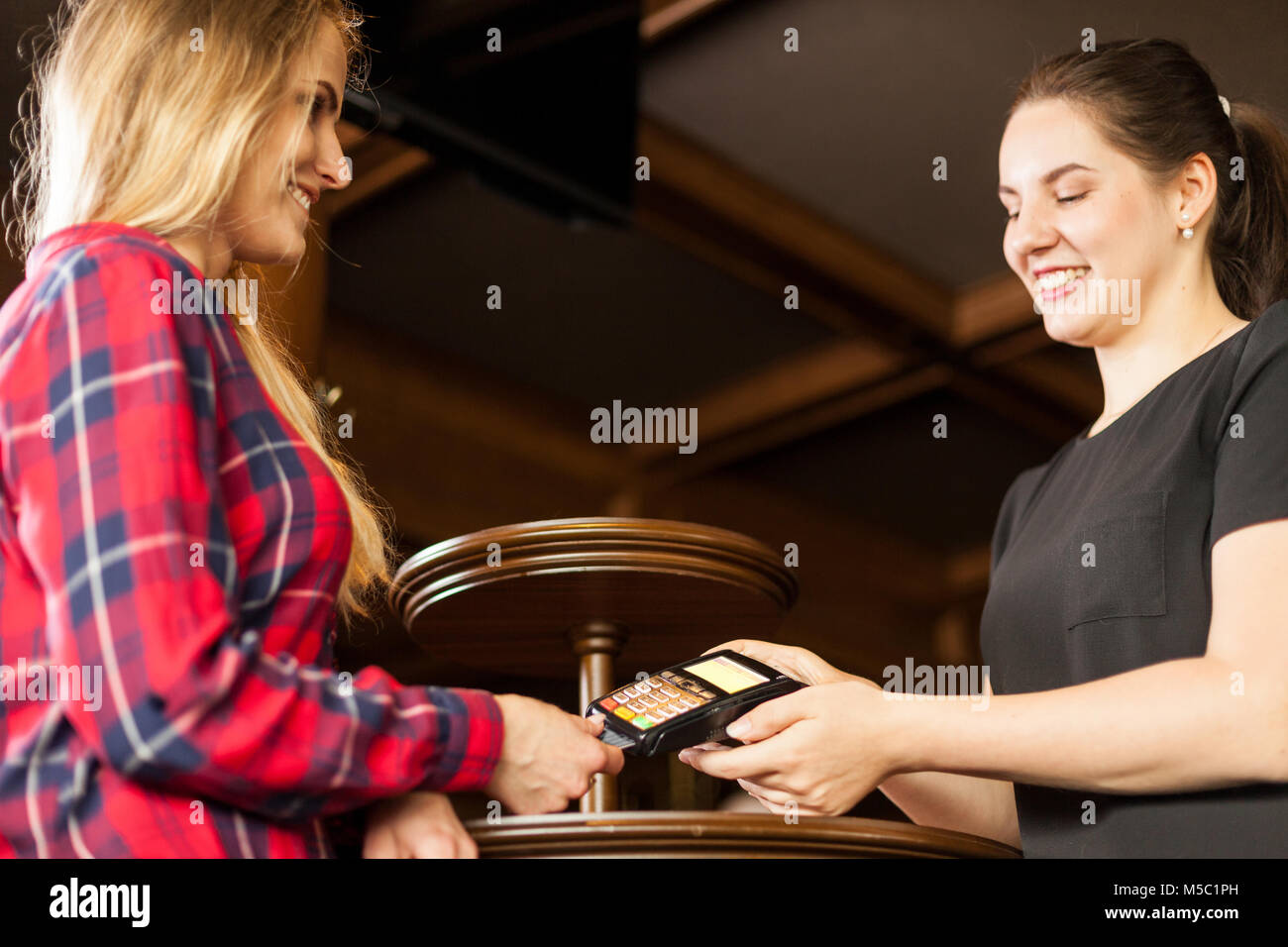 Beautiful smiling cashier receives a payment from a female customer in ...
