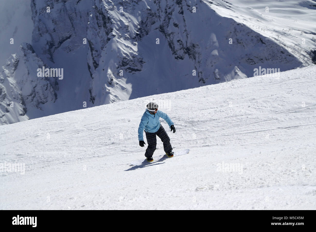 Snowboarder downhill on ski slope in high snowy mountains at sun winter ...