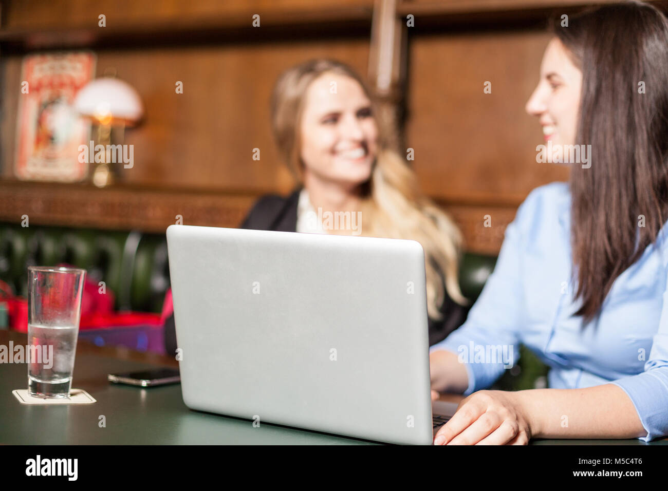 Pretty smiling girls in background working on a computer in foreground ...