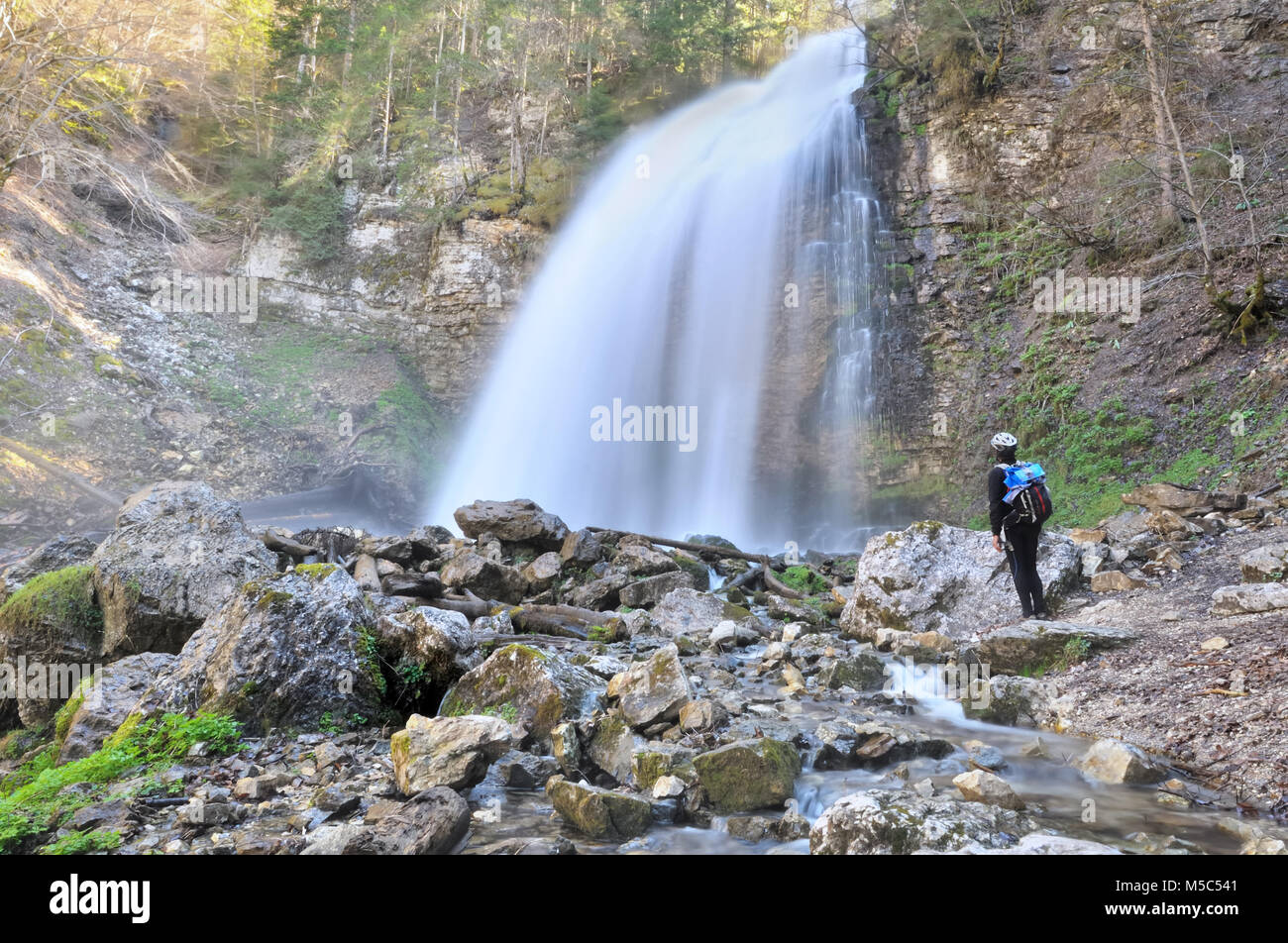 man standing in the feet of a beautiful waterfall in a mountainous ...