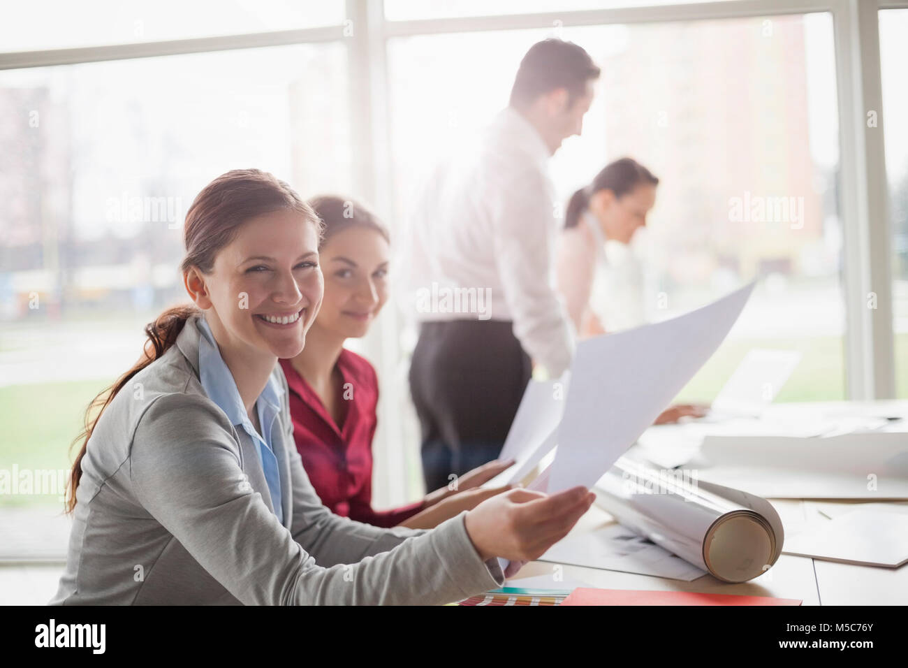 Portrait of smiling young female architects with paperwork at table in ...