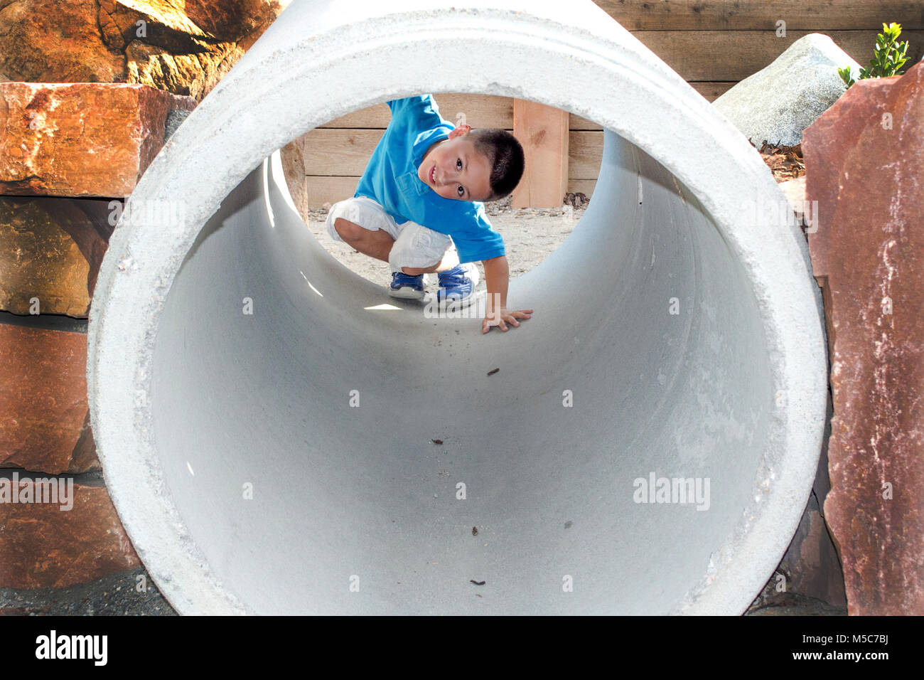 a happy little boy is exploring a very large cement pipe at a children ...