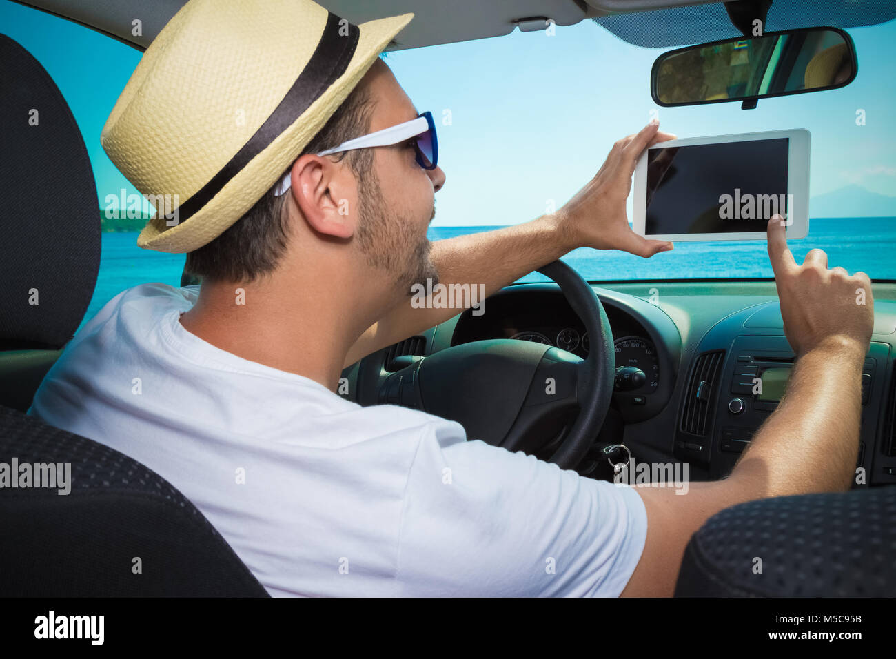 Young car driver touching blank sreen of digital tablet device. Sea in ...