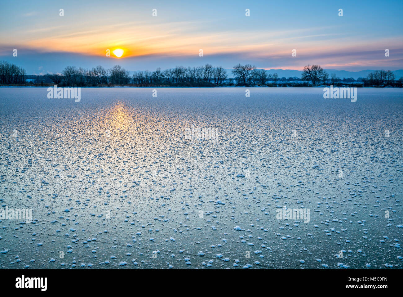 winter sunset over frozen lake and Rocky Mountains in northern Colorado ...