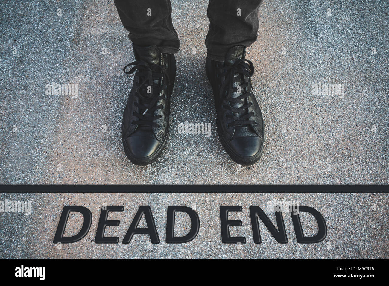 Low section of a person standing with a "dead end" written on the ...