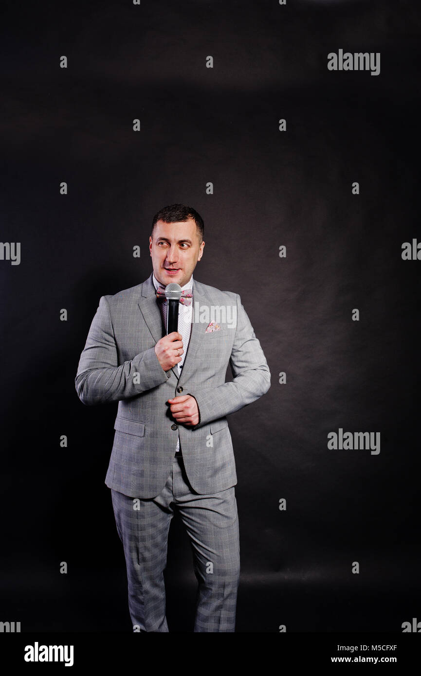 Handsome man in gray suit with microphone against black background on ...
