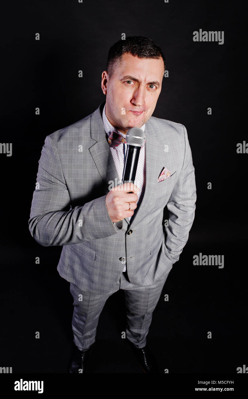 Handsome man in gray suit with microphone against black background on ...