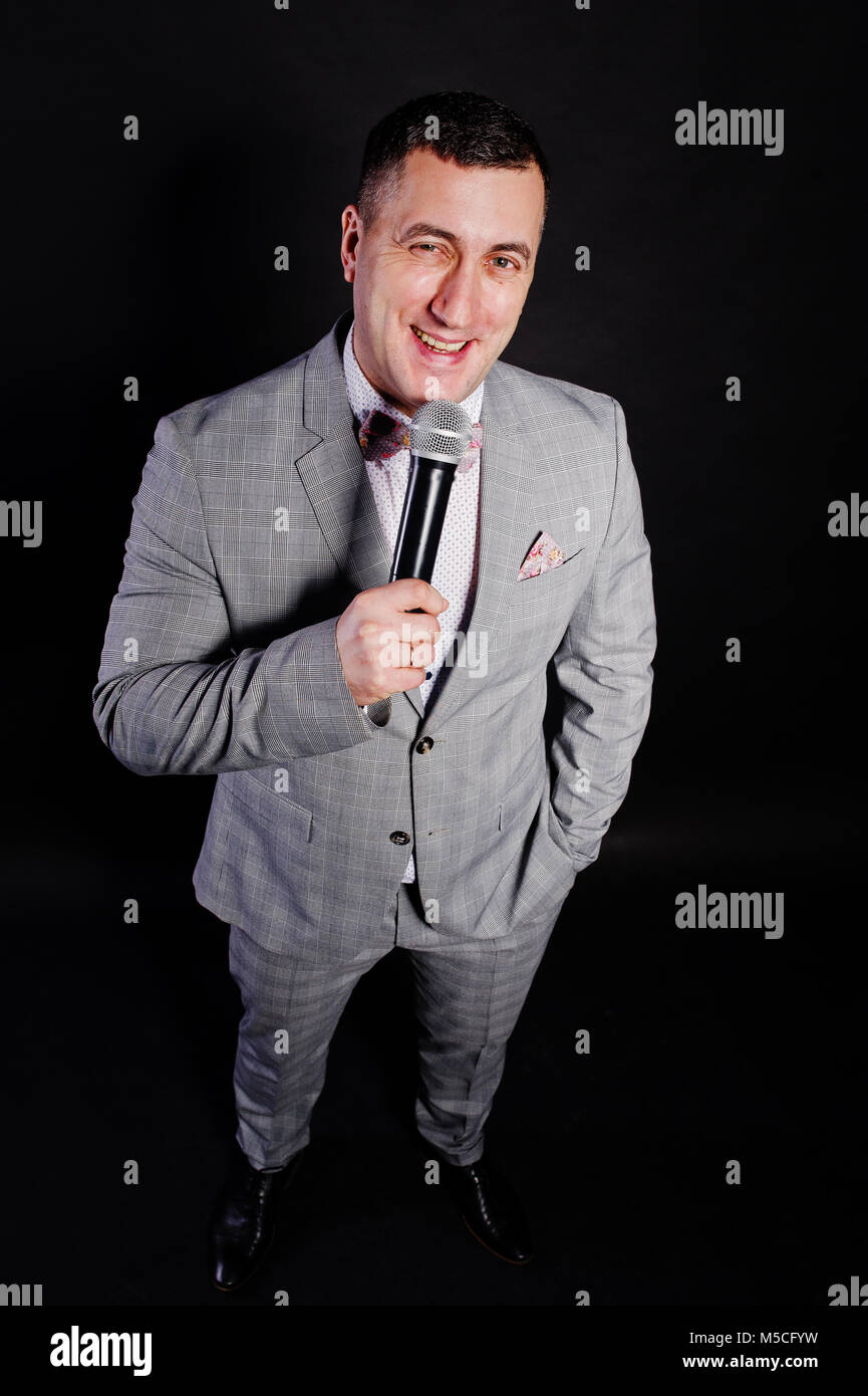 Handsome man in gray suit with microphone against black background on ...