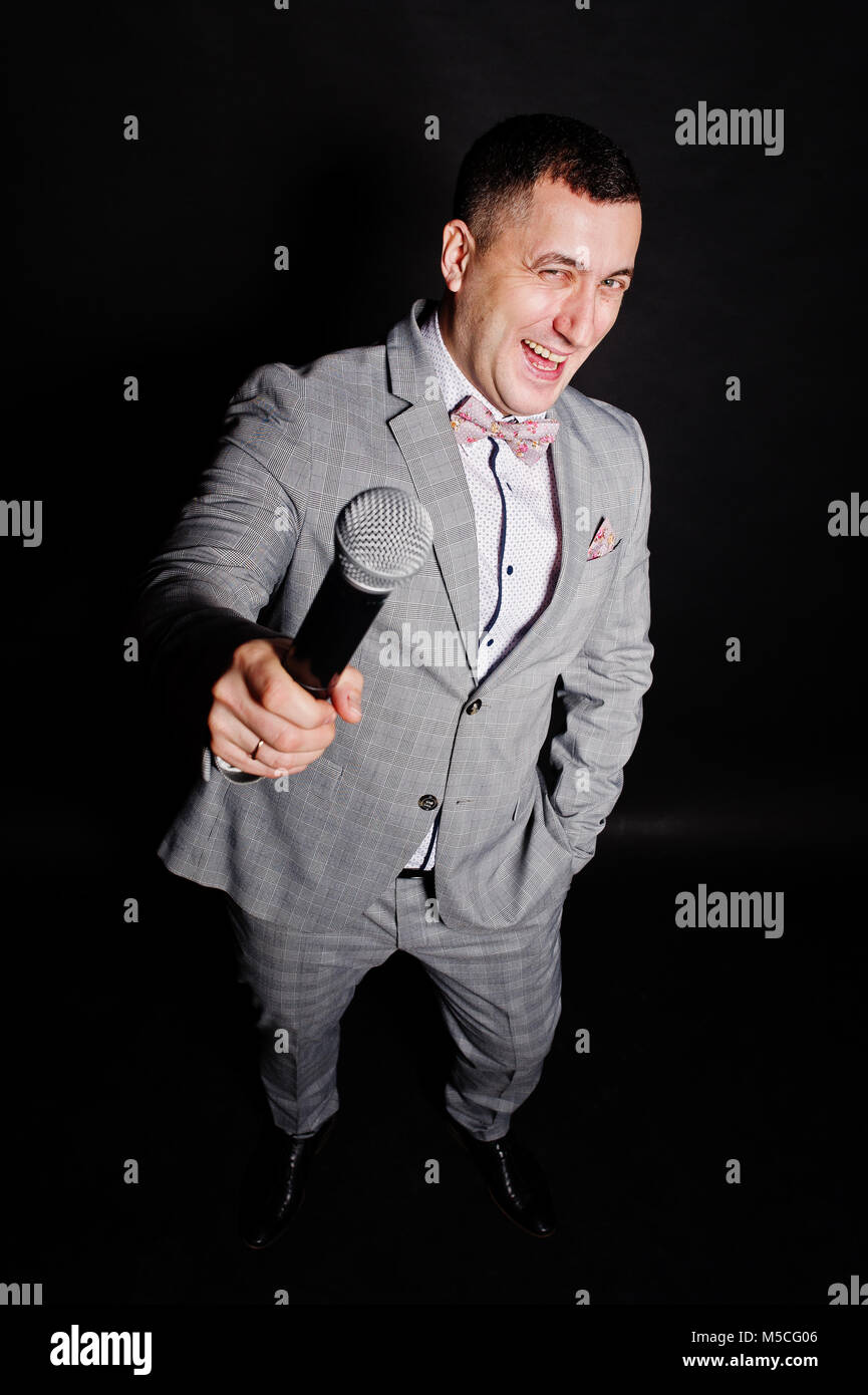 Handsome man in gray suit with microphone against black background on ...