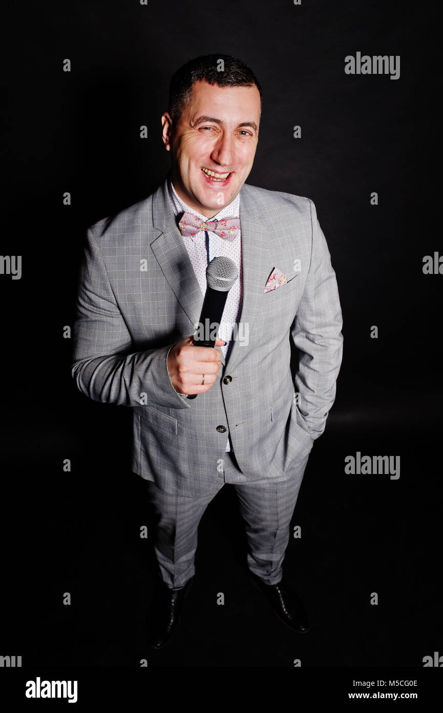 Handsome man in gray suit with microphone against black background on ...