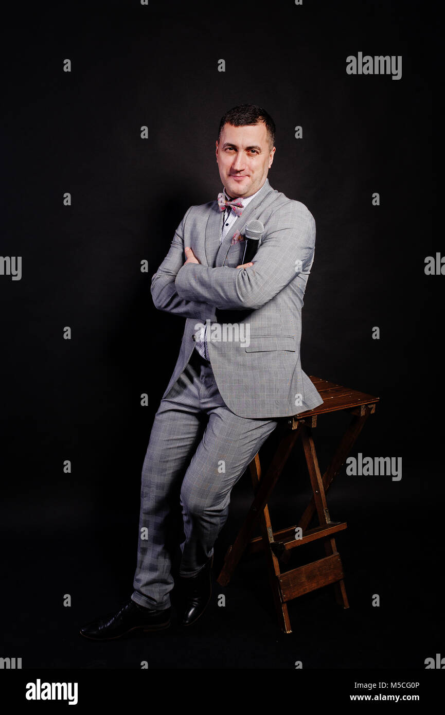 Handsome man in gray suit with microphone against black background on ...