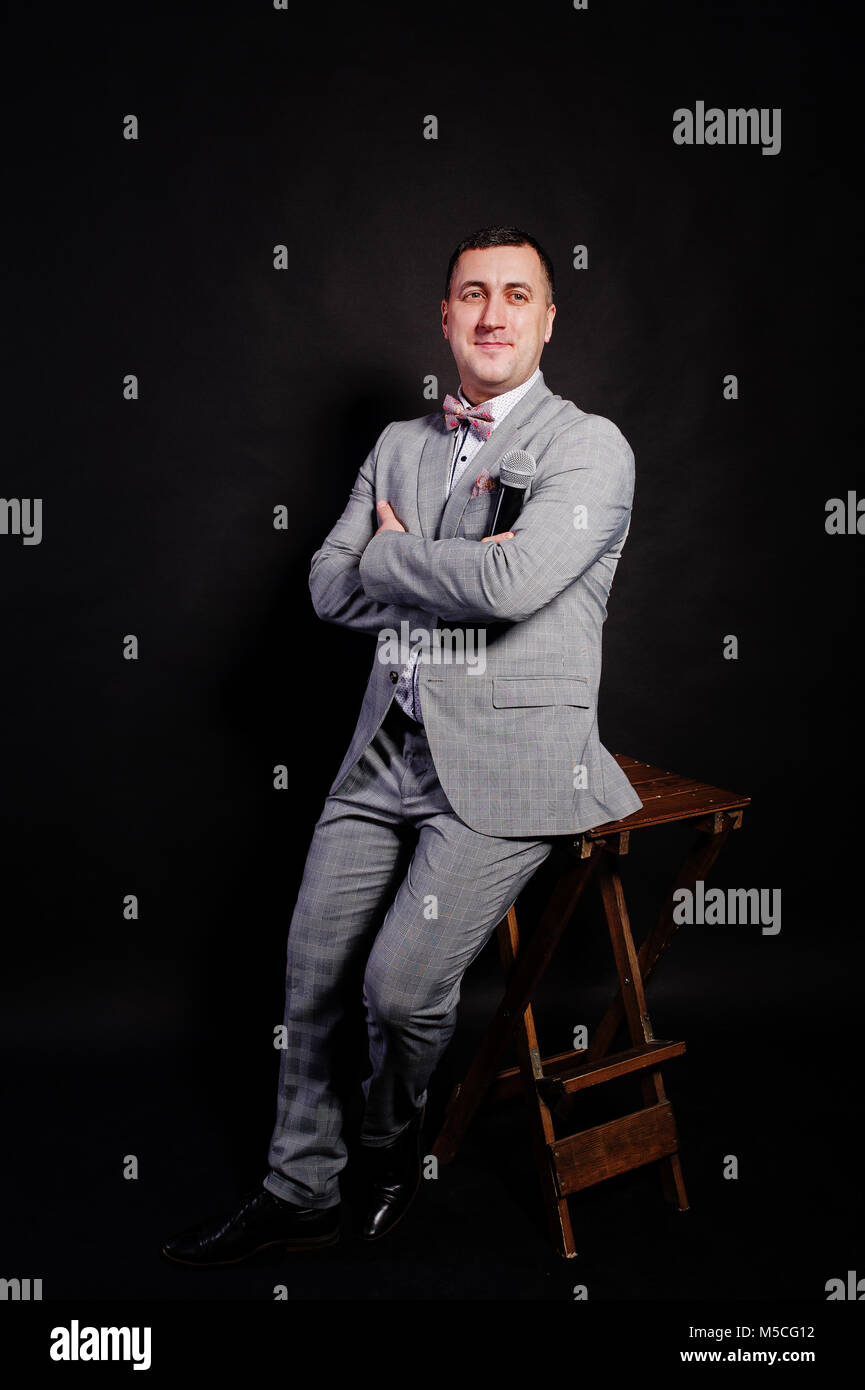Handsome man in gray suit with microphone against black background on ...