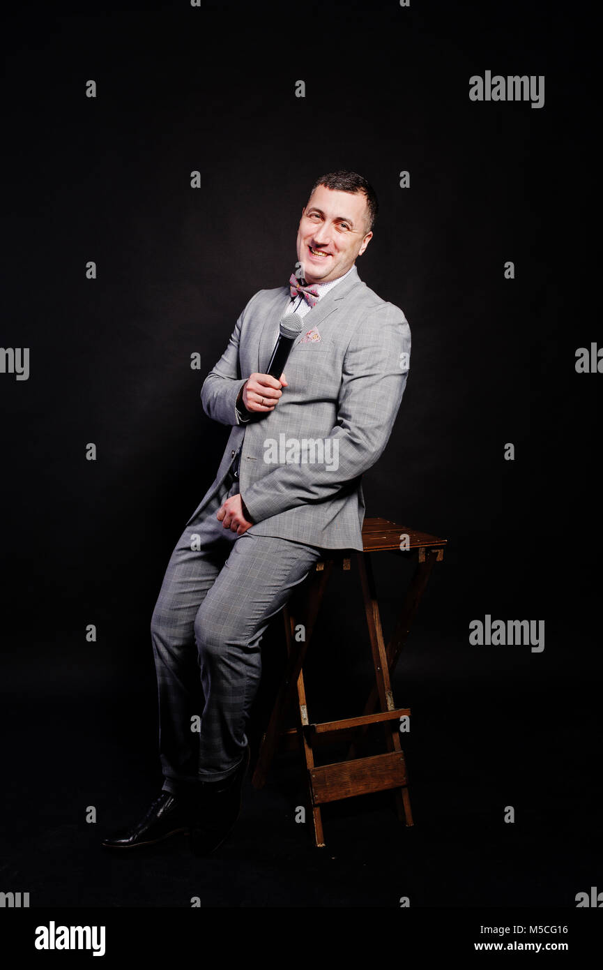 Handsome man in gray suit with microphone against black background on ...