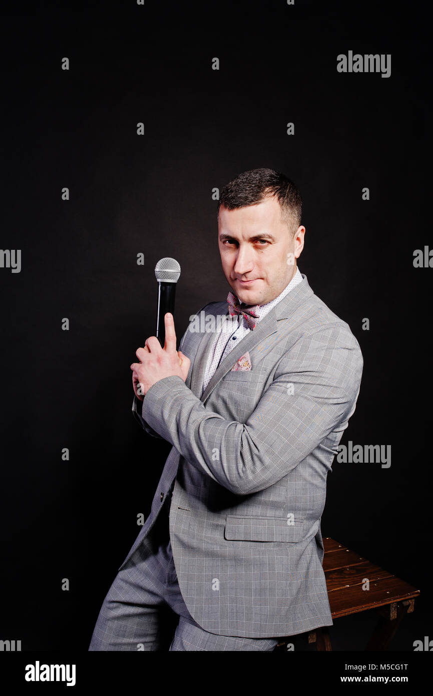 Handsome man in gray suit with microphone against black background on ...