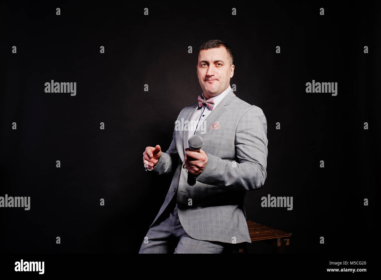 Handsome man in gray suit with microphone against black background on ...