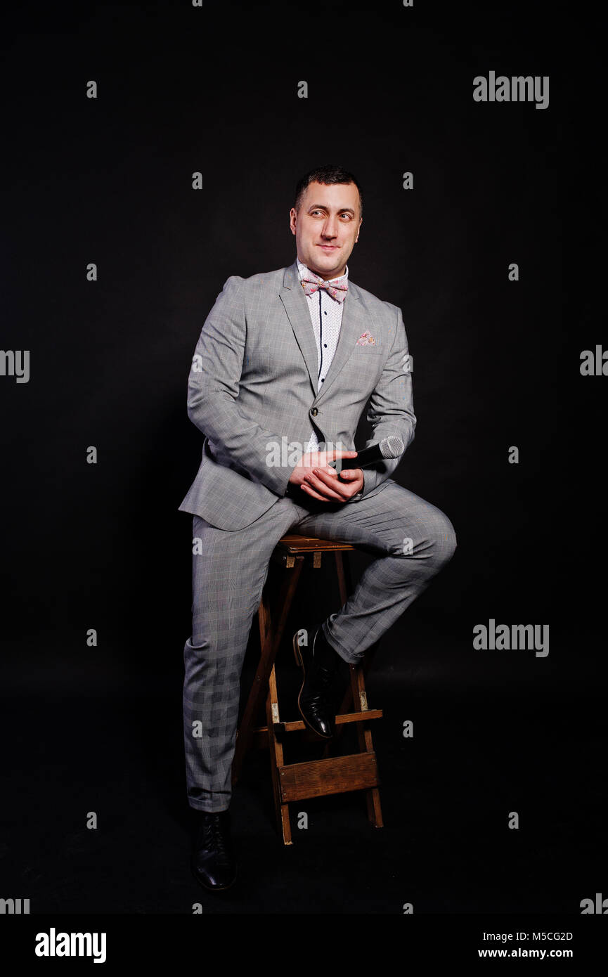 Handsome man in gray suit with microphone against black background on ...