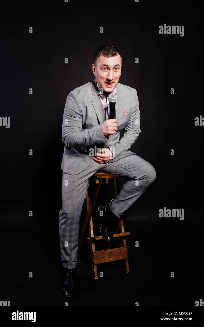 Handsome man in gray suit with microphone against black background on ...